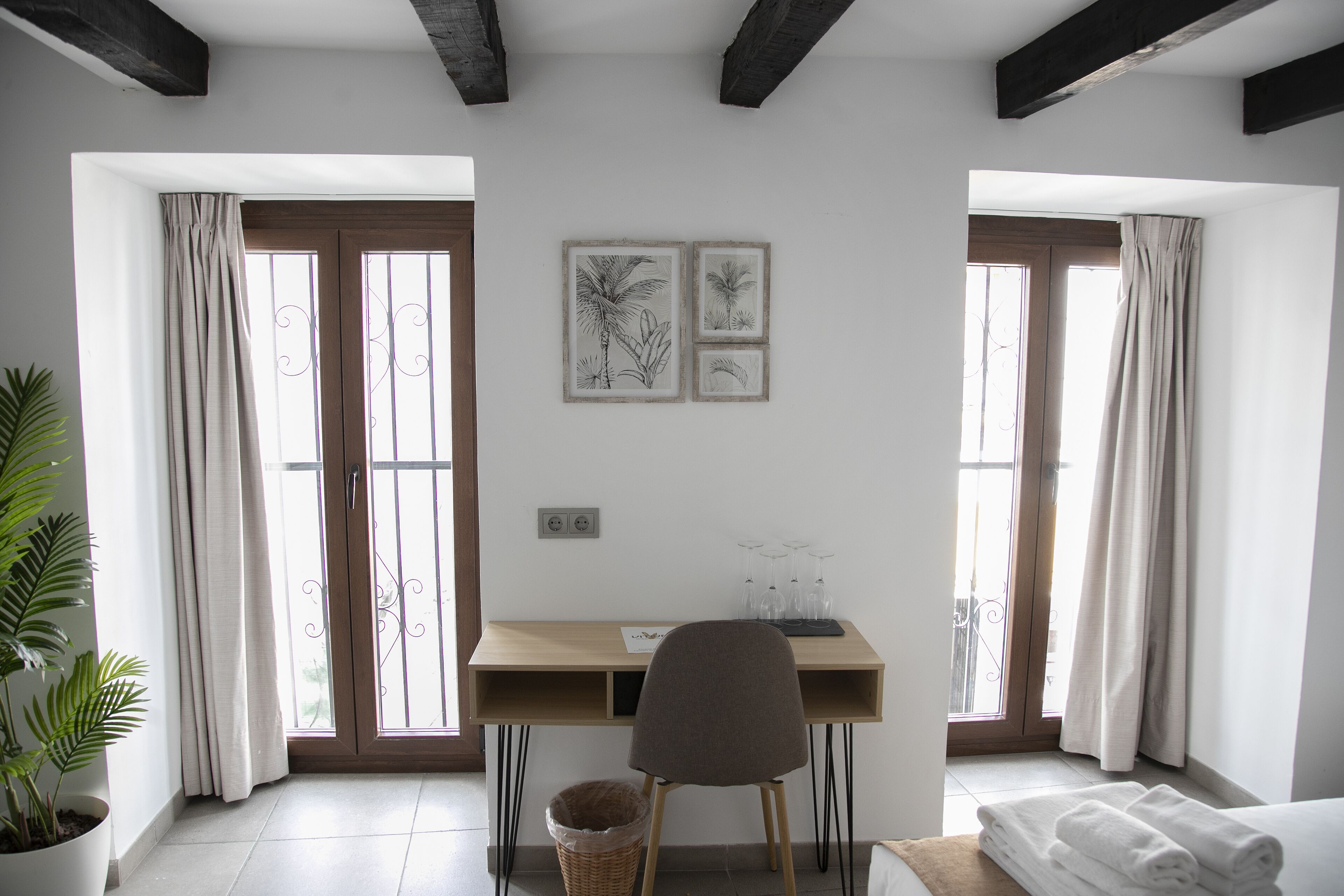Quarto com escrivaninha de madeira, uma cadeira, um vaso com planta e janela com cortinas.