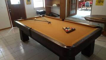 Uma mesa de bilhar com bolas, uma porta, uma janela e uma prateleira com objetos.