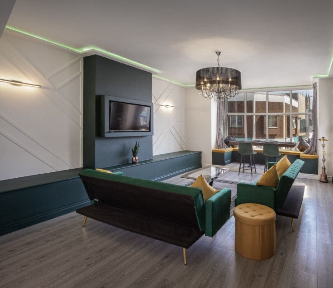 Uma sala de estar moderna com televisão de tela plana, sofás verdes, um banquinho de madeira e um candelabro.