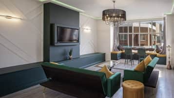Uma sala de estar moderna com televisão de tela plana, sofás verdes, um banquinho de madeira e um candelabro.