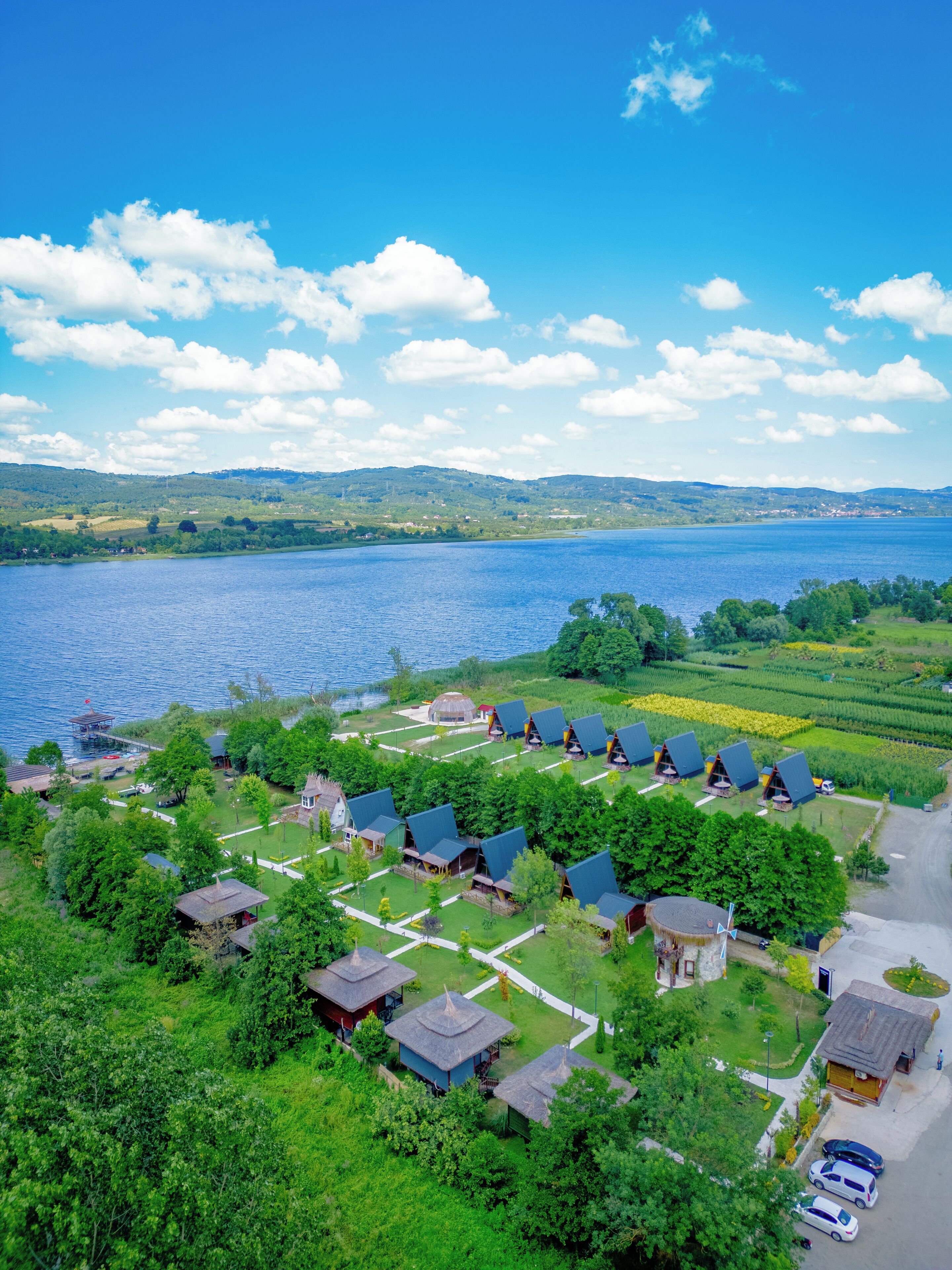Vista aérea de um resort à beira do lago, com várias cabanas, um moinho de vento e um píer.