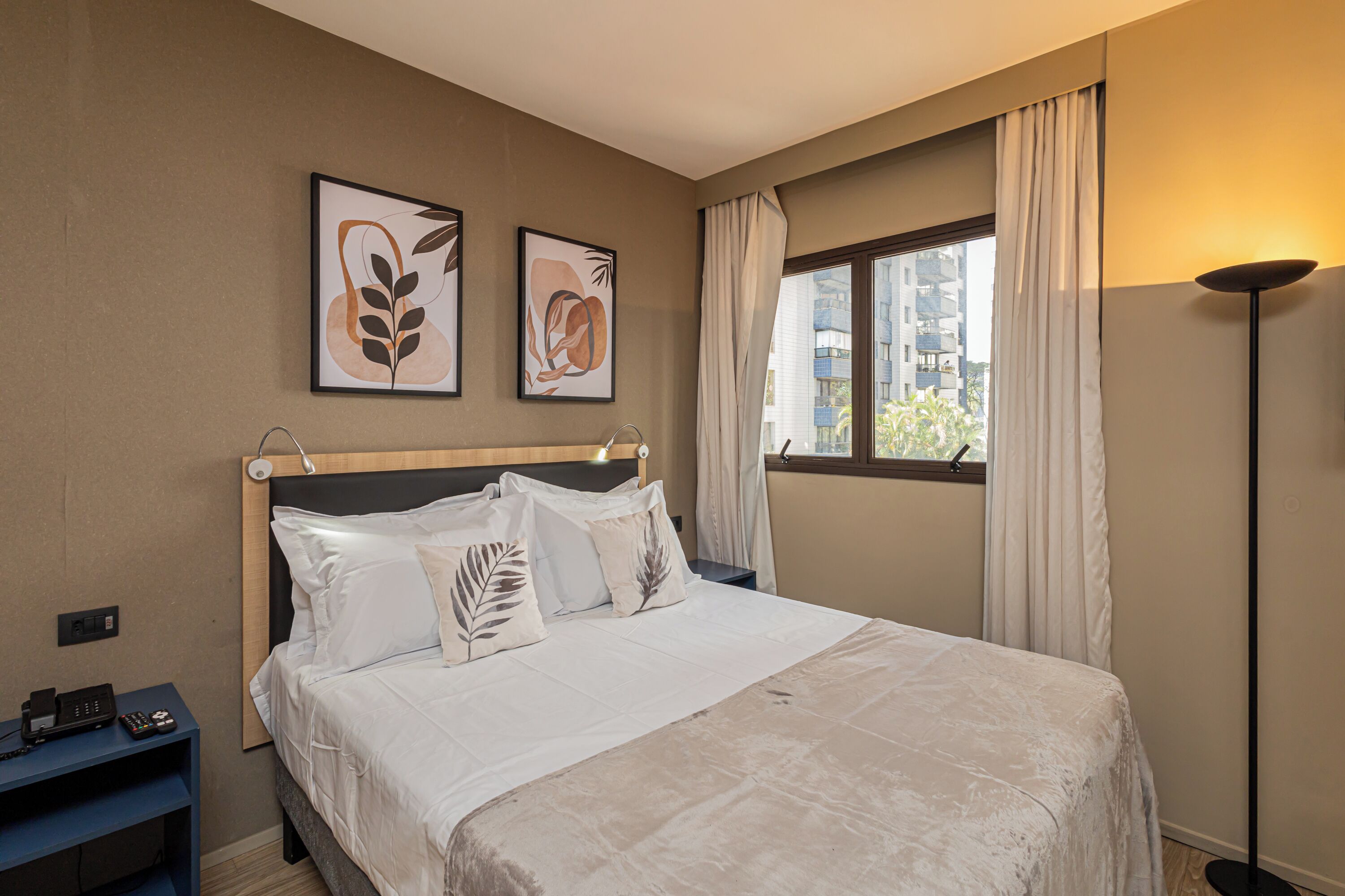 Quarto de hotel com uma cama, uma mesa de cabeceira e um telefone, e uma janela com cortinas.