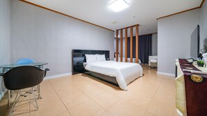 Quarto de hotel com cama, escrivaninha, cadeira, televisão e uma pequena mesa com uma planta.