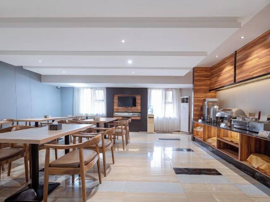Uma ampla área de refeições com várias mesas e cadeiras, bancada de cozinha com eletrodomésticos e uma tela grande na parede.
