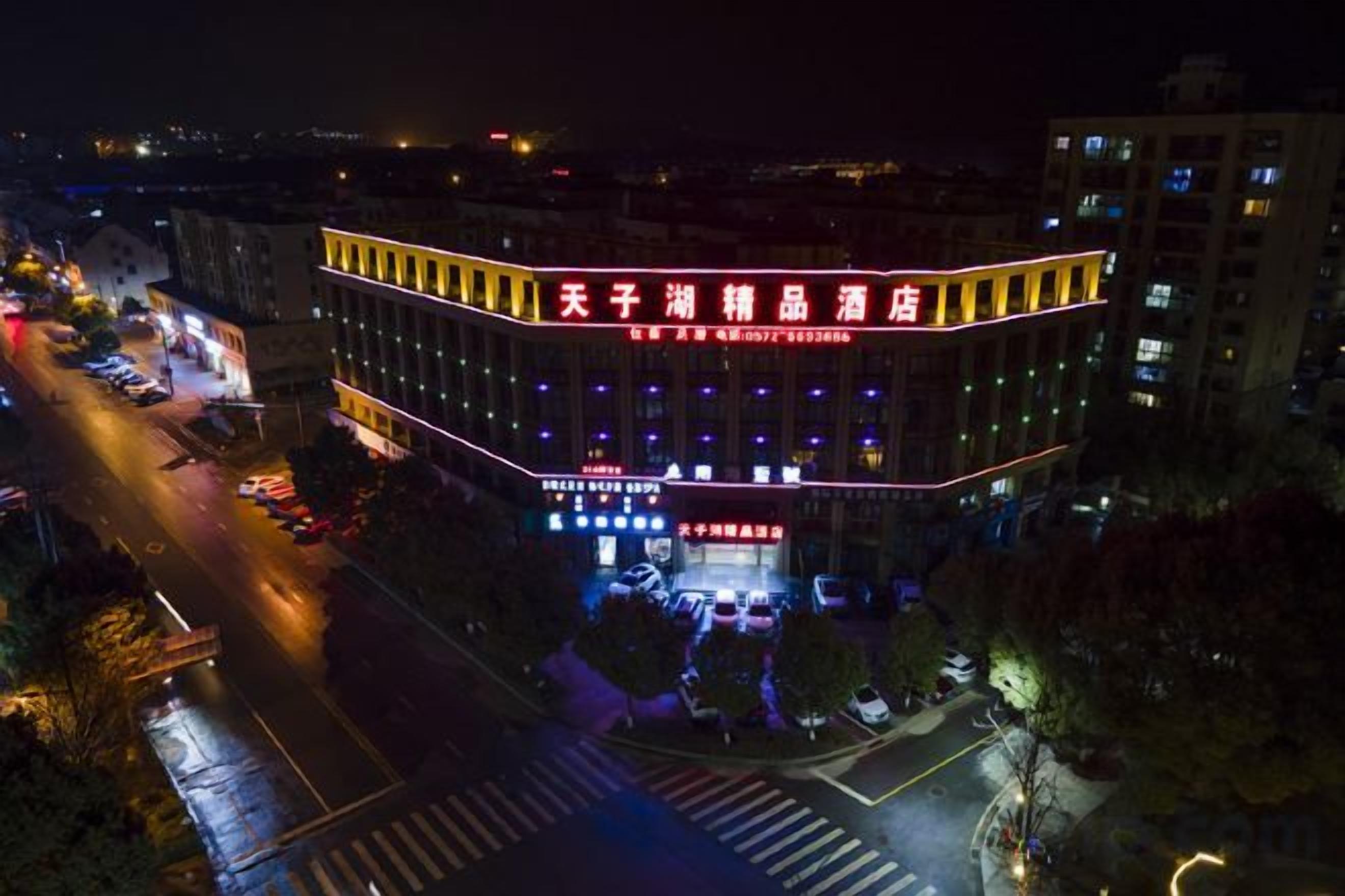 Hotel com vários andares, placa chamativa, estacionamento e faixa de pedestres em frente.