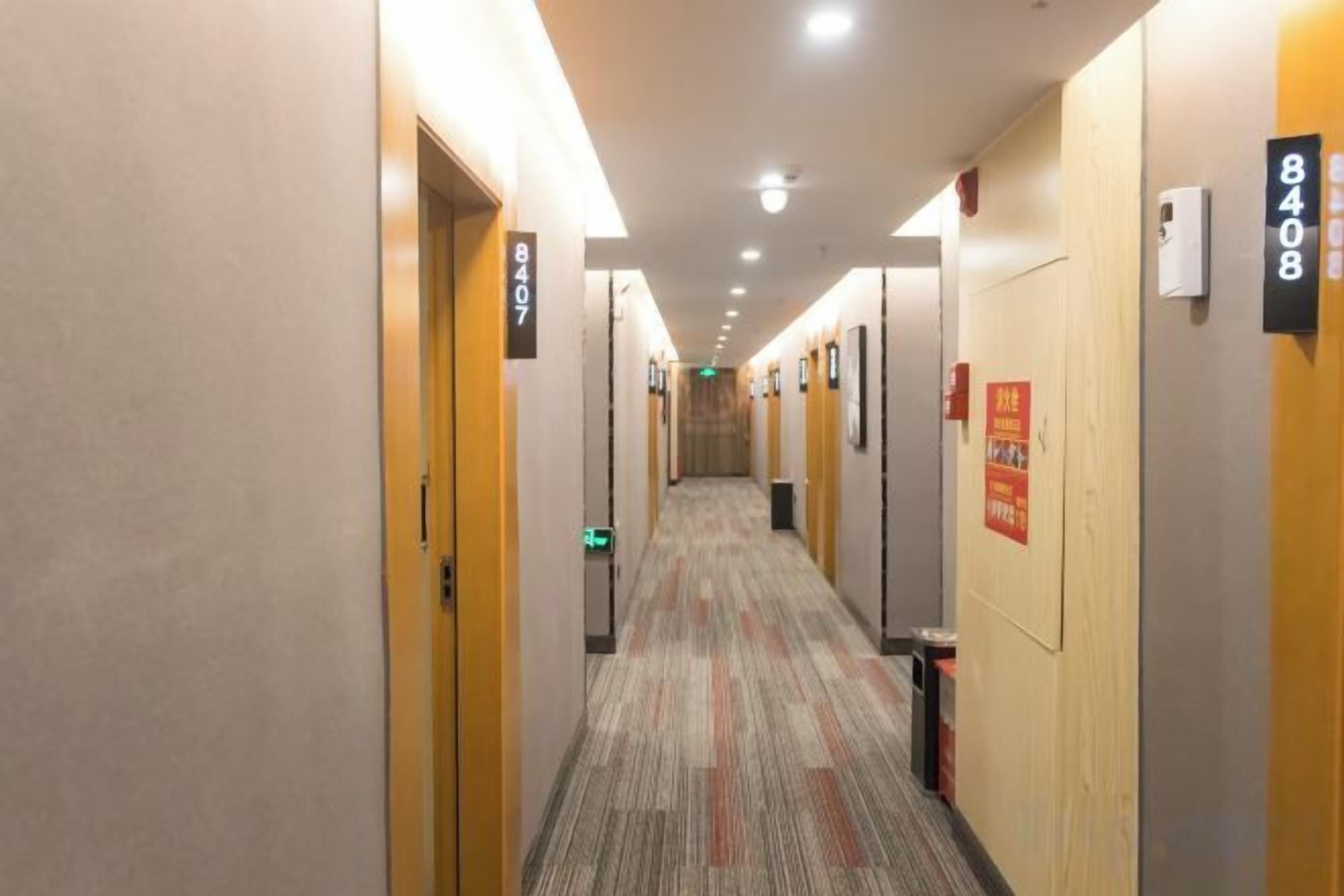 Corredor de hotel com portas numeradas 8407 e 8408, piso coberto por carpete e placas de saída de emergência.