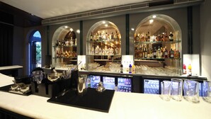 Uma área de bar com prateleiras cheias de garrafas de bebidas, copos e um balcão com um tapete preto e utensílios de bar.