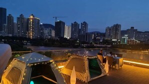 Terraço no telhado com tendas e uma mesa, com vista para o horizonte urbano ao entardecer.