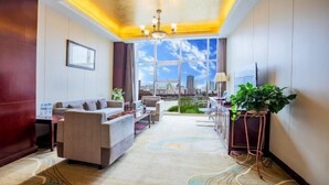 Quarto de hotel com sofá, mesa pequena, planta em vaso, vista da cidade e um candelabro.