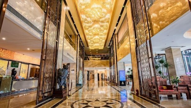 Um hall de hotel luxuoso, com piso de mármore polido, divisórias de madeira ornamentadas e um imponente candelabro.