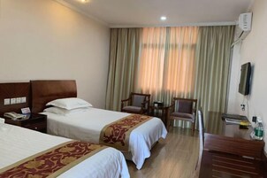 Quarto de hotel com duas camas, uma escrivaninha, uma cadeira, uma televisão e uma janela com cortinas.