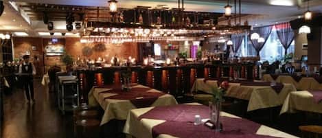 Um restaurante com várias mesas, um espaço de bar e luminárias pendentes.