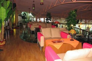 Um espaço amplo e arejado com piso de madeira, diversos arranjos de assentos incluindo sofás e poltronas, e várias plantas em vasos.