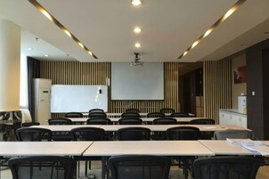 Sala de conferência com quadro branco, projetor e fileiras de mesas e cadeiras.