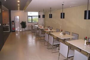 Uma sala de jantar moderna com várias mesas e cadeiras, uma geladeira e um distribuidor automático.