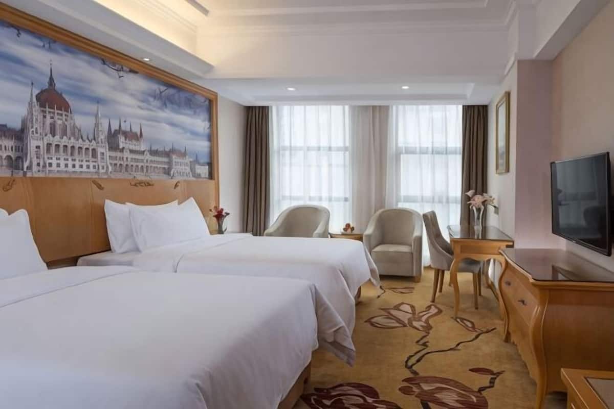 Quarto de hotel com duas camas, uma televisão, uma escrivaninha e uma cadeira.