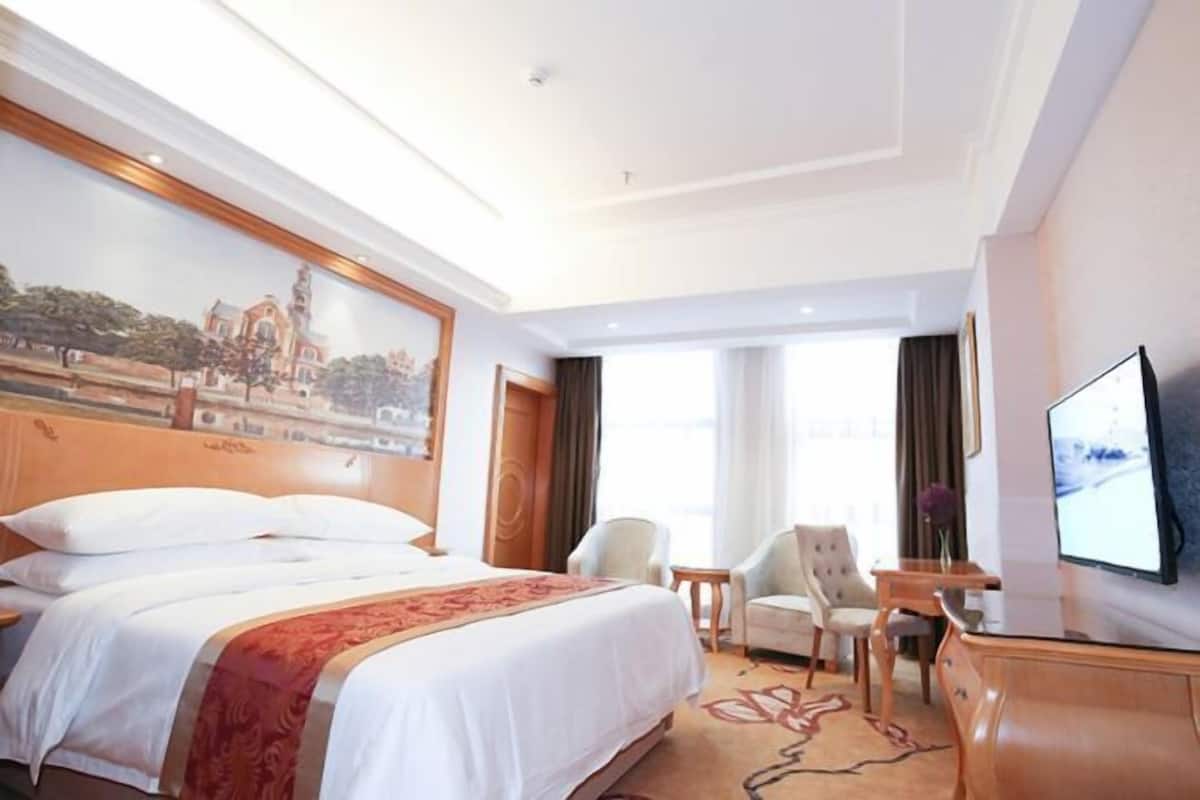 Quarto de hotel com uma cama grande, uma escrivaninha, uma cadeira e uma televisão.