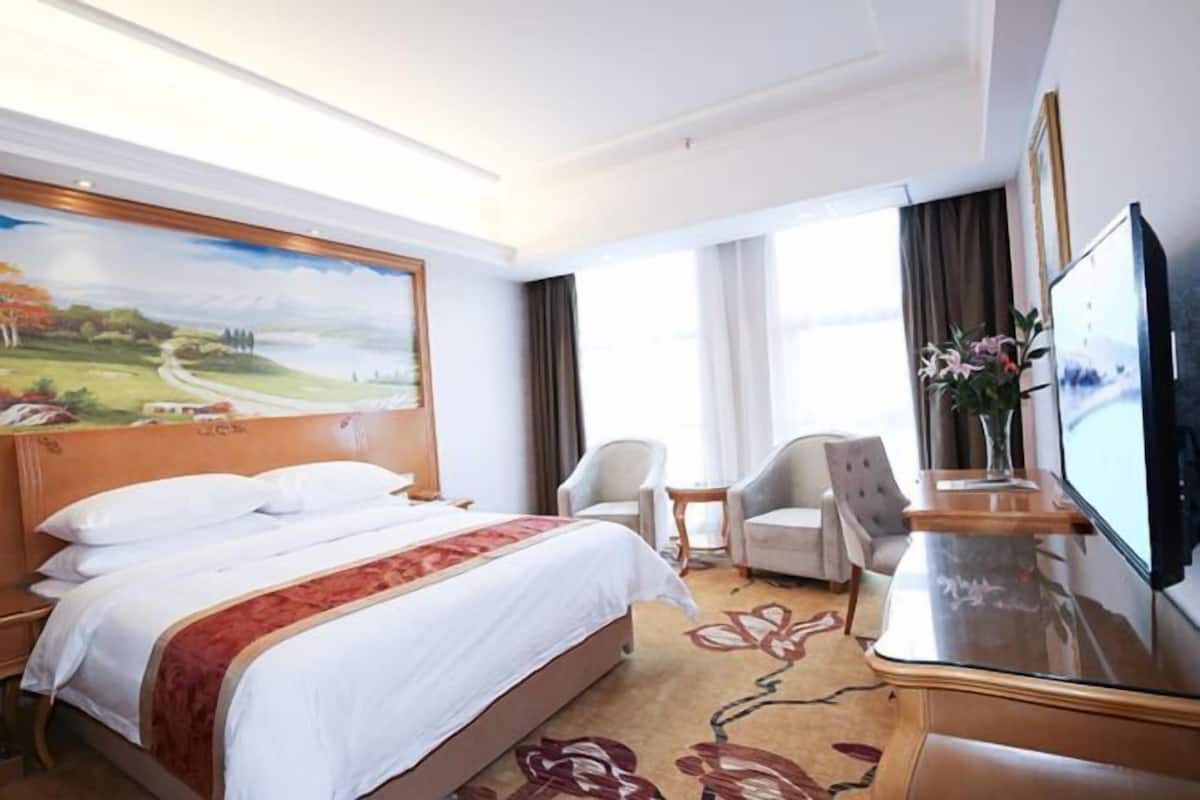 Quarto de hotel com uma cama grande, televisão, escrivaninha e uma cadeira.