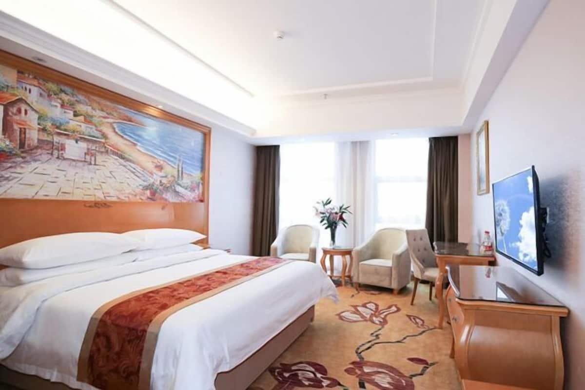 Quarto de hotel com uma cama grande, uma escrivaninha, uma cadeira, uma televisão e um quadro na parede.