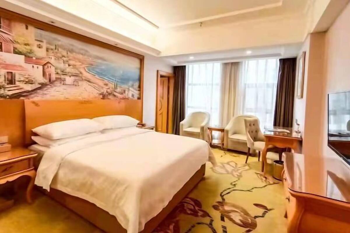 Quarto de hotel com uma cama grande, uma mesa, duas cadeiras e um quadro na parede.