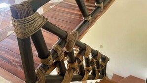A staircase with a wooden handrail wrapped in rope, leading to a room with a bed and a window overlooking greenery.