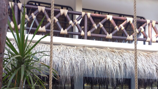 Uma área de piscina com telhado de palha, cordas e deck de madeira.