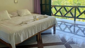 A hotel room with a bed, a painting, a thermostat, and a view of greenery through a window.