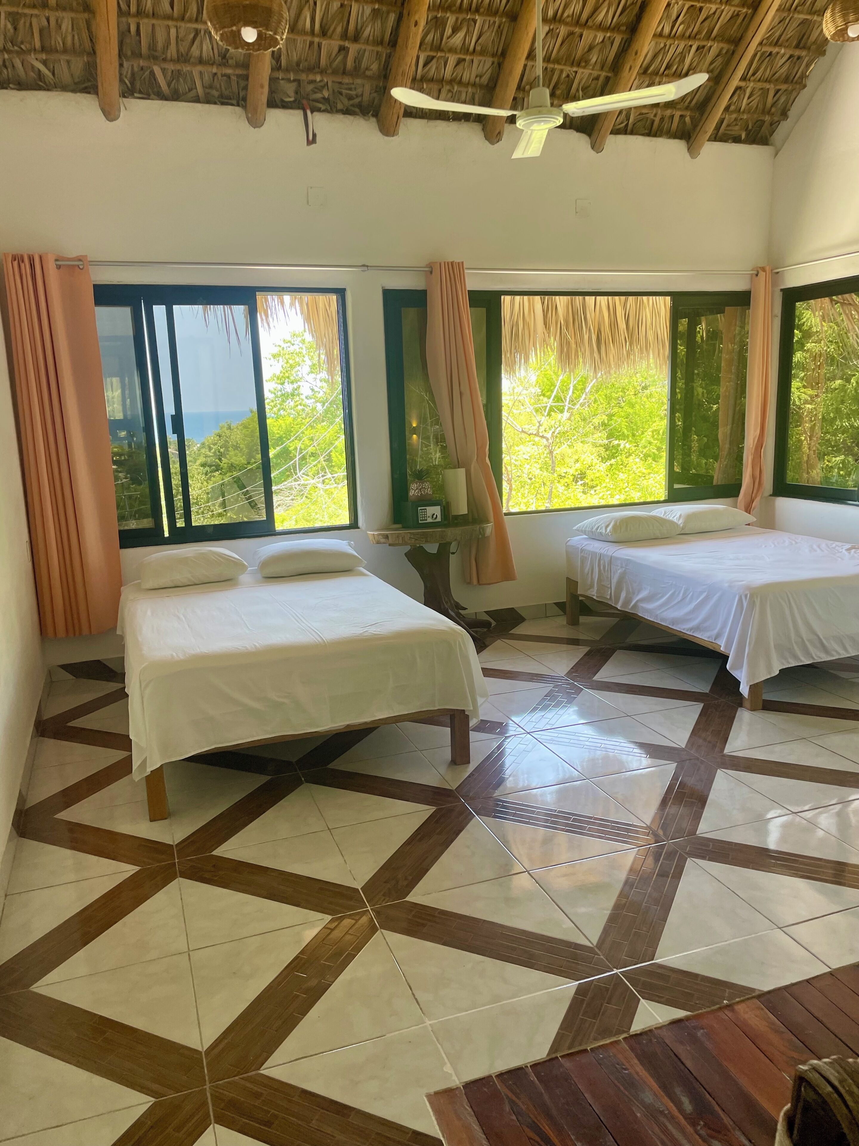 Quarto com duas camas, ventoinha no teto e vista para o verde lá fora.