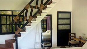 A hotel room with a staircase, a bed, a chair, a table, and a window.