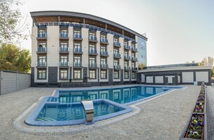 Um hotel moderno com fachada curva, piscina e área de jardim florida.