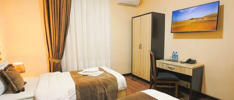 Quarto de hotel com duas camas, uma escrivaninha, uma cadeira, ar condicionado e um quadro na parede.