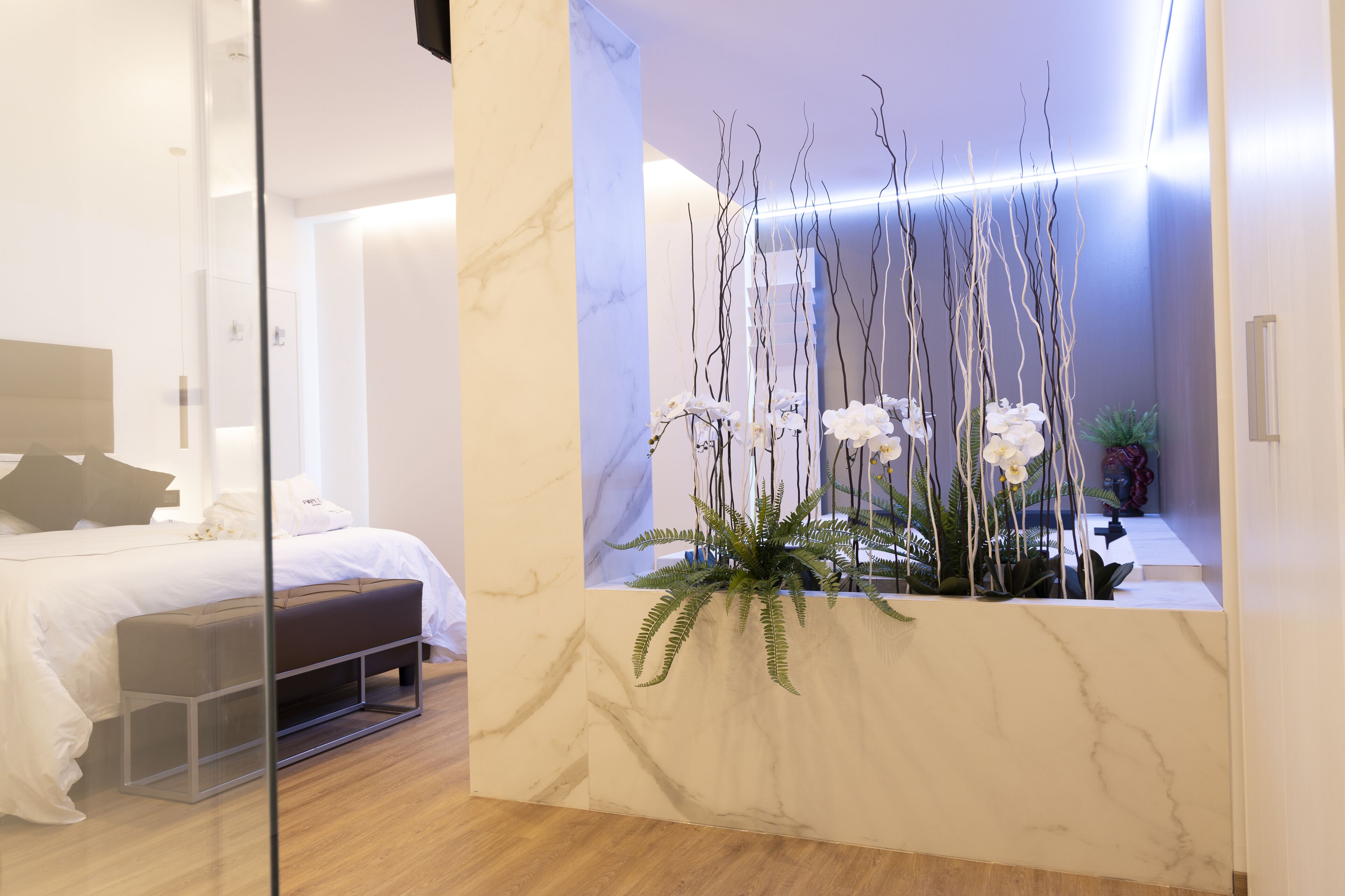 Quarto moderno com cama, um banquinho e uma parede verde com orquídeas.