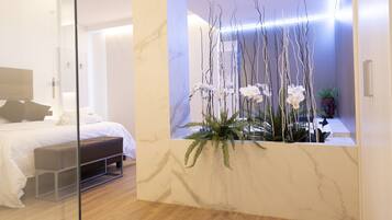Quarto moderno com cama, um banquinho e uma parede verde com orquídeas.