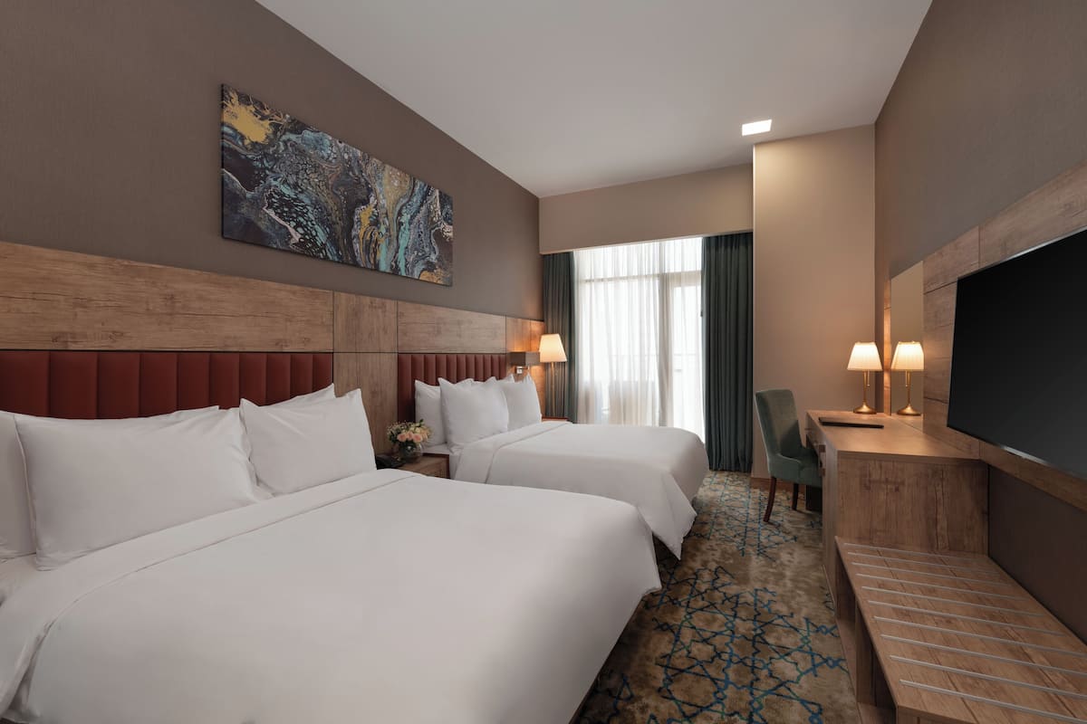 Quarto de hotel com duas camas, uma mesa de trabalho com uma televisão e um quadro abstrato grande na parede.