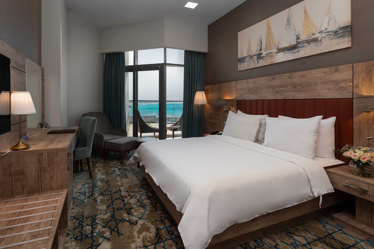 Quarto de hotel com uma cama grande, uma escrivaninha, uma cadeira, uma televisão e vista para o mar.