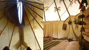 Uma tenda com um mastro central e cordas, uma cama com um cobertor listrado, e decorações nas paredes, incluindo uma estrela e enfeites pendurados.