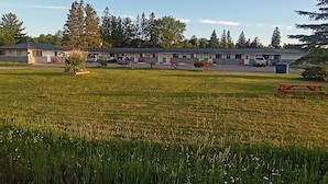 Um motel com uma fileira de quartos, estacionamento e uma mesa de piquenique em um campo gramado.