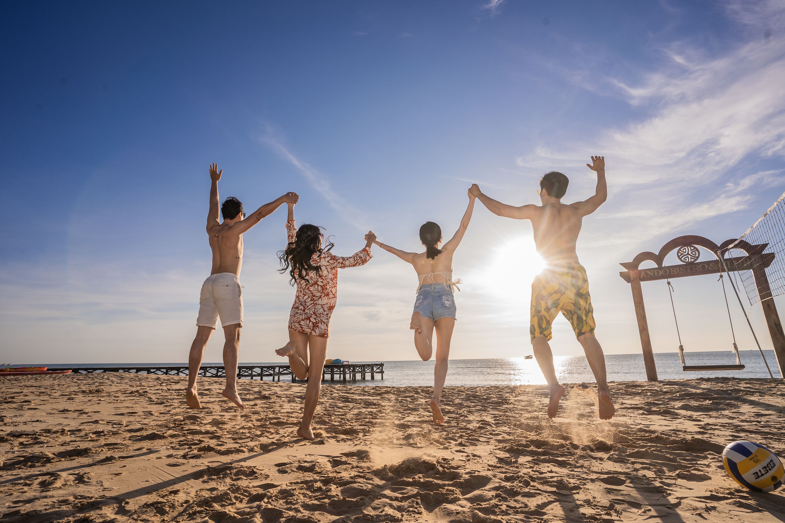 Uma praia com uma rede de voleibol e um cais ao fundo.