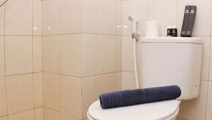 Sanitário com toalha azul no assento, chuveiro e produtos de higiene no reservatório.