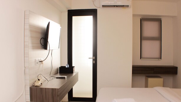 Quarto de hotel com cama, mesa de cabeceira, TV fixada na parede e porta para o exterior.