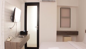Quarto de hotel com toucador de madeira, televisão de ecrã plano na parede, cama com edredão branco e janela com vista.