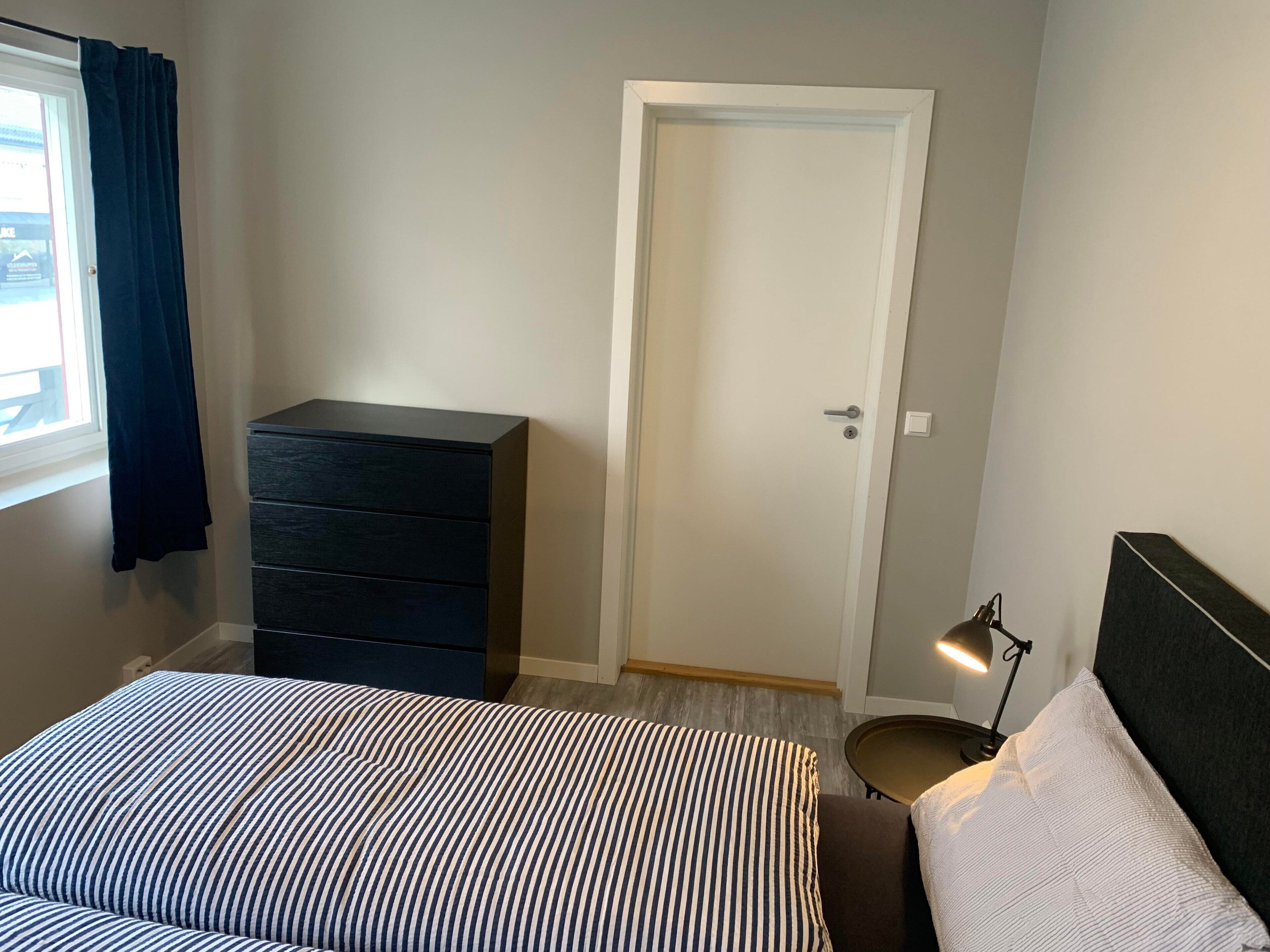 Quarto com cama, penteadeira, porta e abajur.