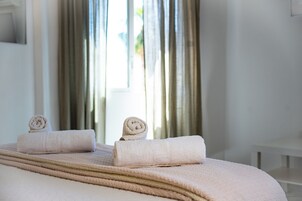 Cama bem arrumada com toalhas dobradas, cabeceira branca e janela com cortinas.