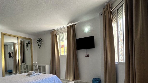 Quarto de hotel com uma cama, uma cadeira, uma televisão e uma janela com cortinas.