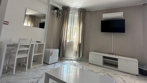 Uma sala de estar moderna com um rack branco para TV, uma televisão de tela plana, uma mesa de jantar branca e uma geladeira branca.