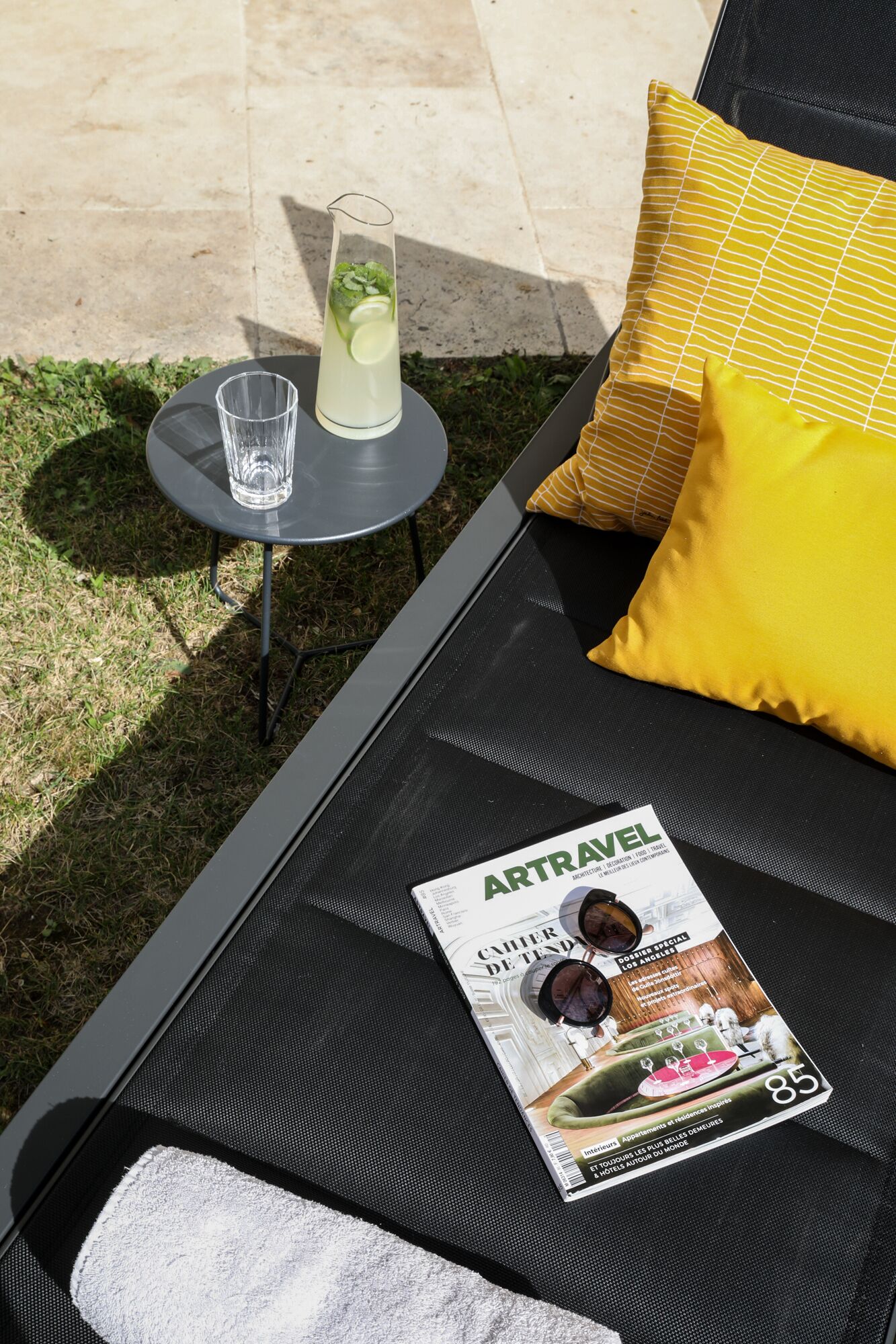 Uma área de estar com uma revista, um copo de bebida e uma almofada amarela.