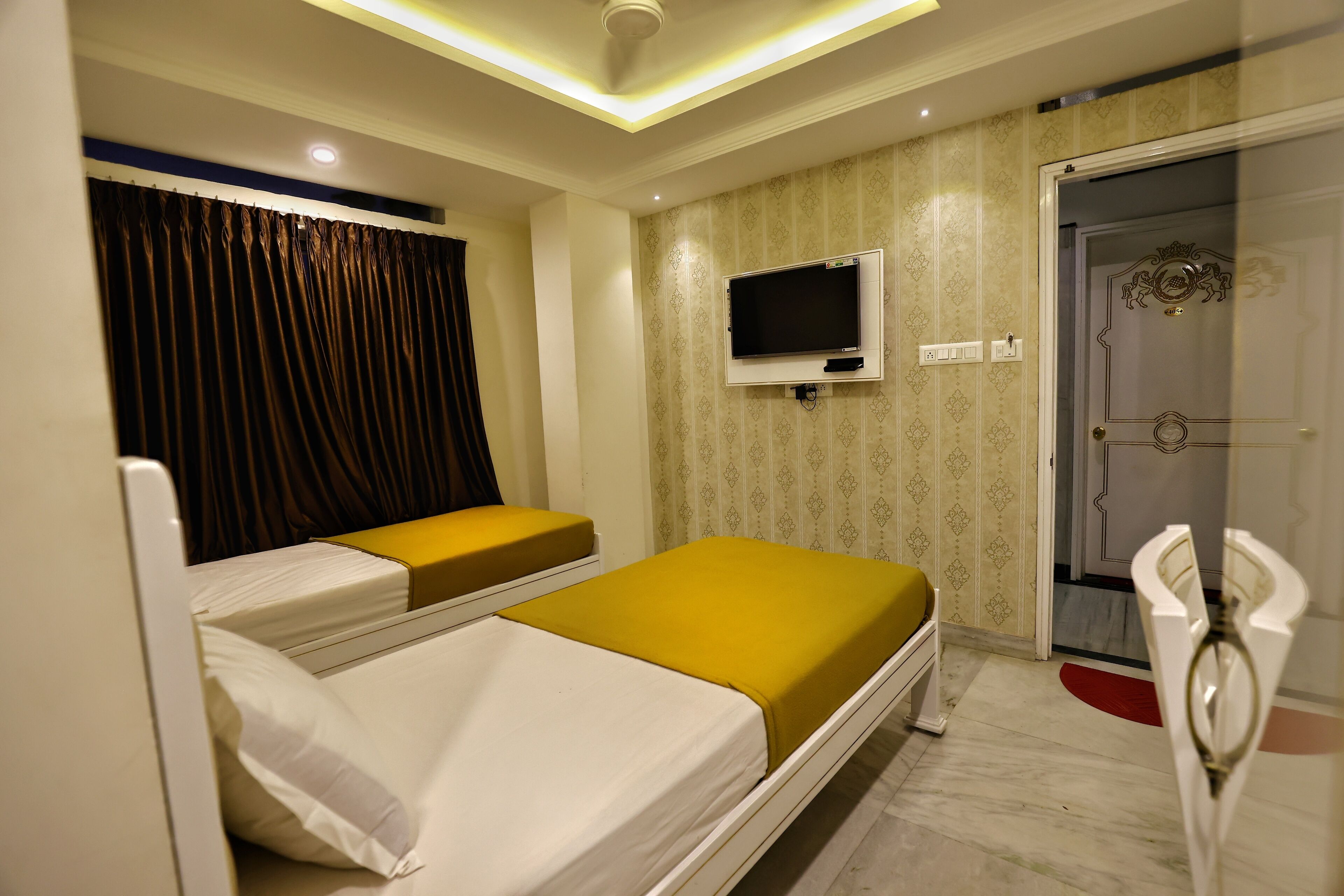 Quarto de hotel com duas camas, televisão, chuveiro e porta com puxador decorativo.