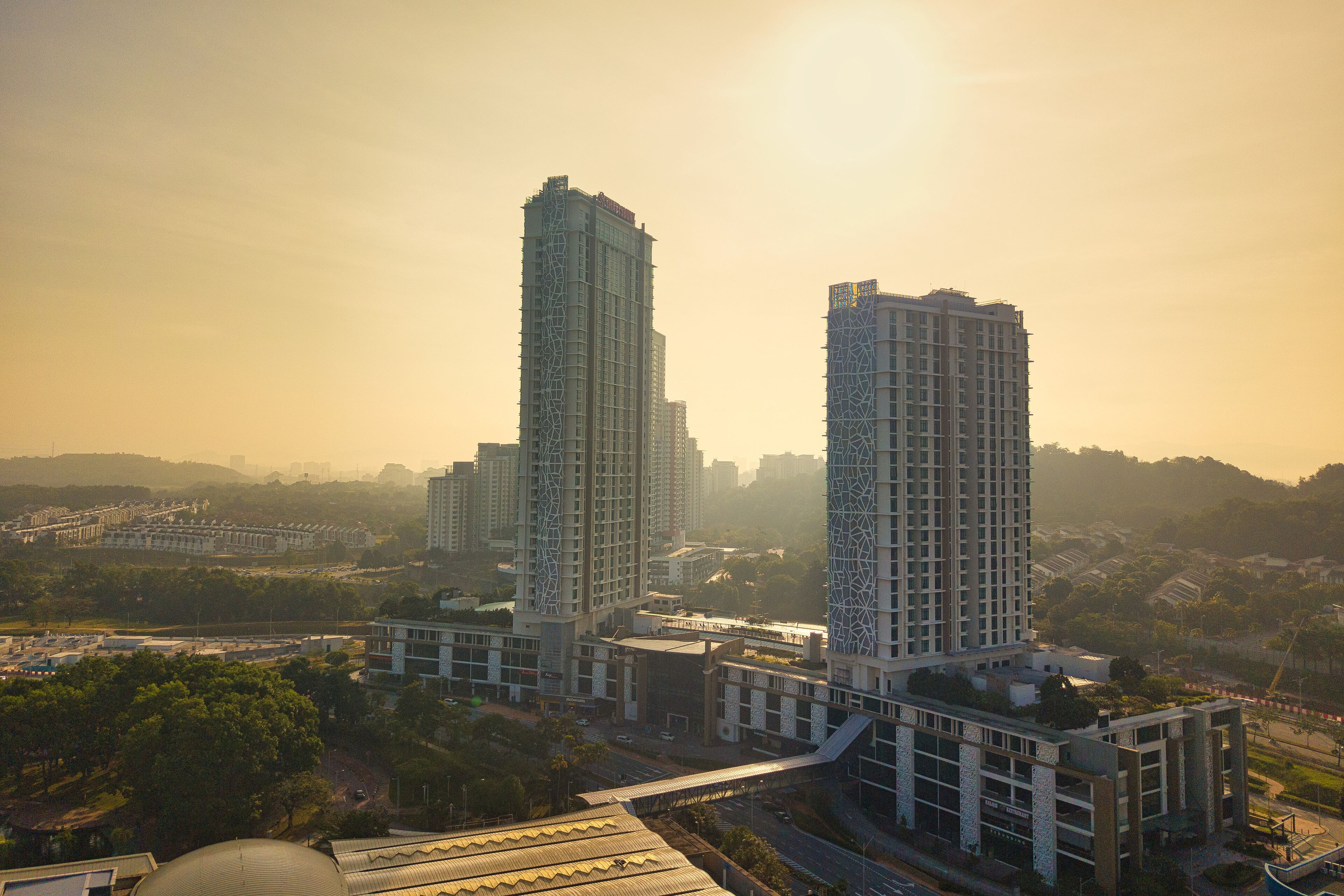 Um edifício alto com design arquitetônico moderno, cercado por vegetação e outros edifícios.