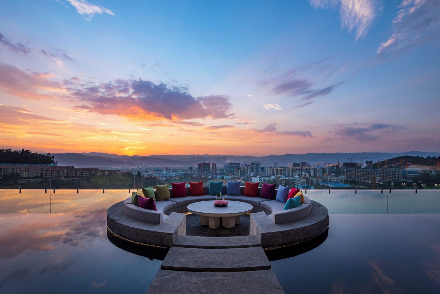 Terraço no telhado com área de estar circular e vista para a cidade ao pôr do sol.