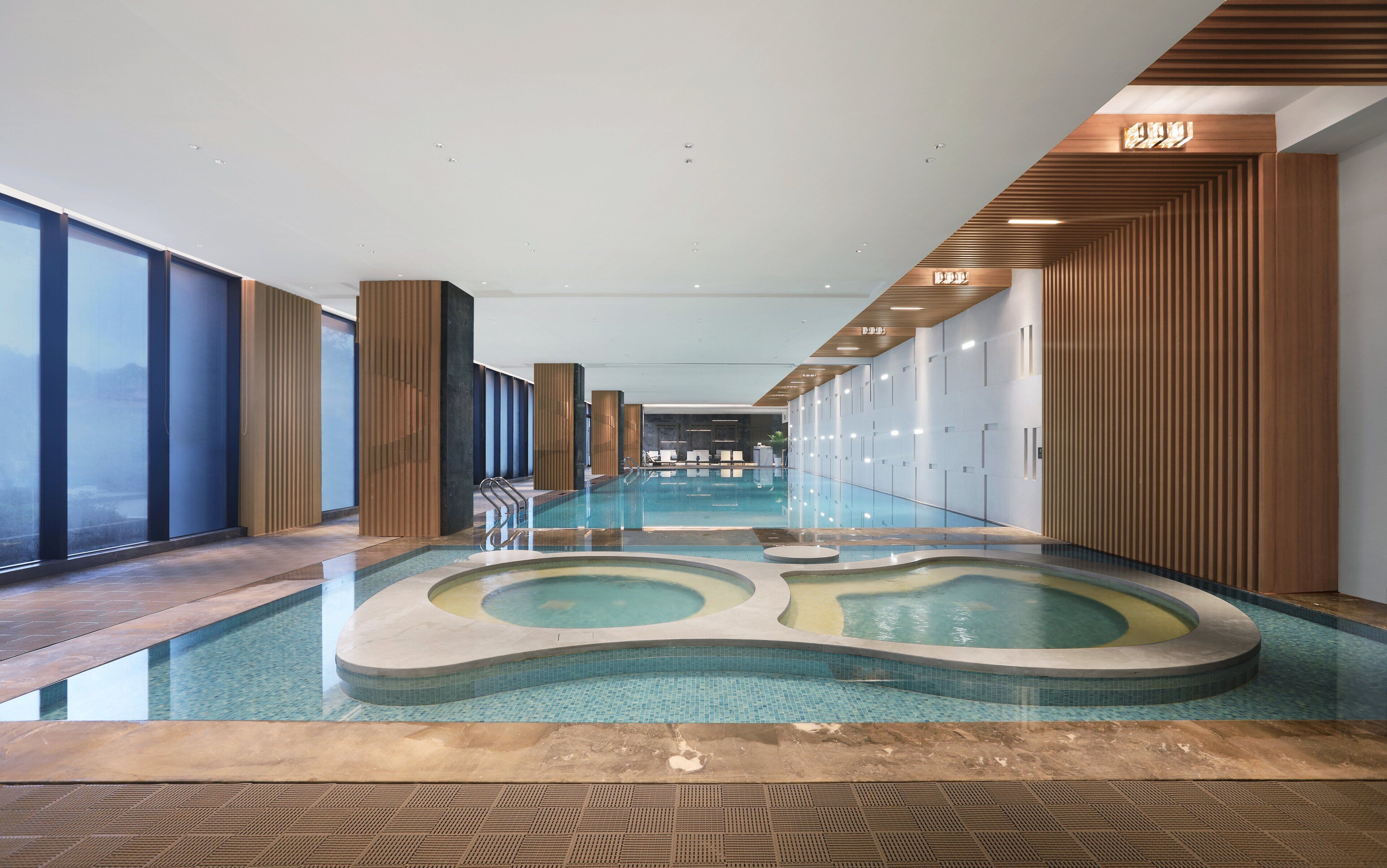 Um saguão de hotel moderno com área de piscina central, com várias fontes e assentos.